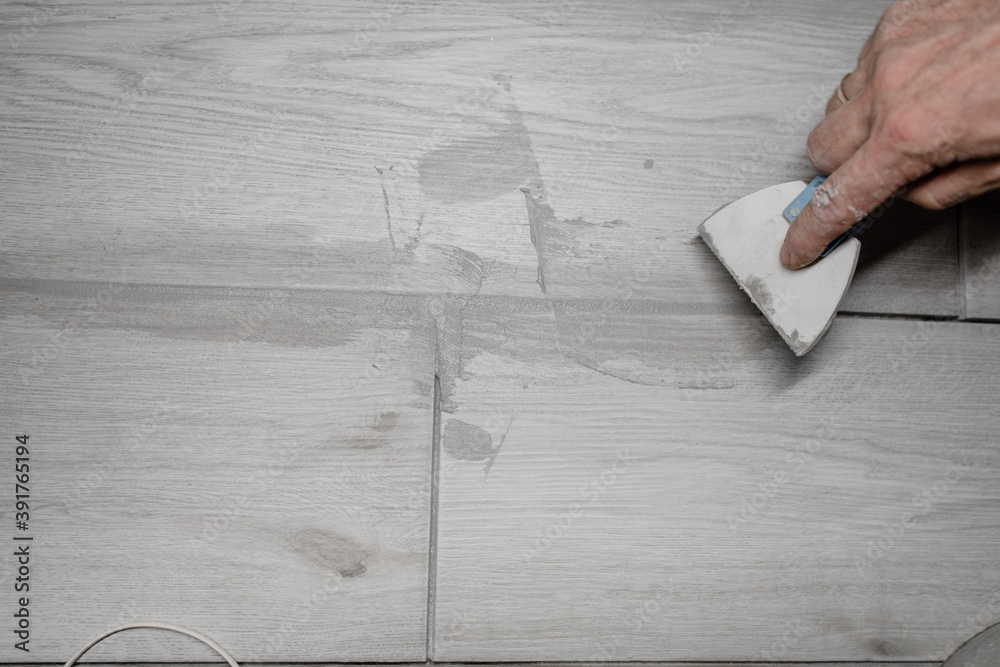 jointing of floor tiles. Grouting tiles seams with a rubber trowel ...