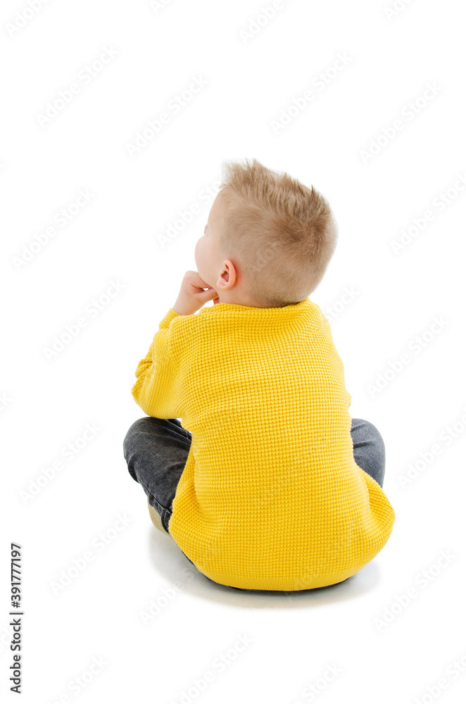 Back view of little boy sitting on floor looking side at copy space ...