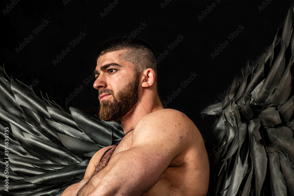 handsome physically well-developed man with black angel wings on a dark ...
