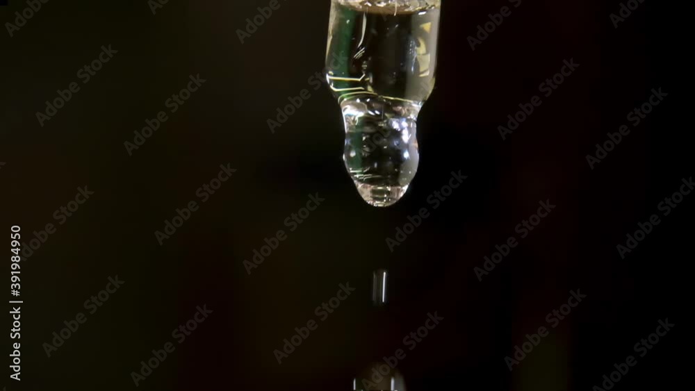 Styling liquid drop drips from transparent glass pipette against black ...