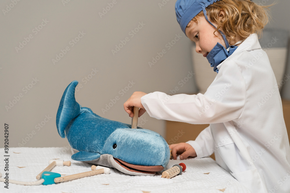 young child wearing medical PPE examines a plush toy whale by taking ...