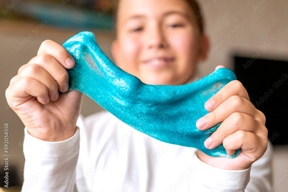 Girl stretching blue glitter slime to the sides. Kids hands playing ...
