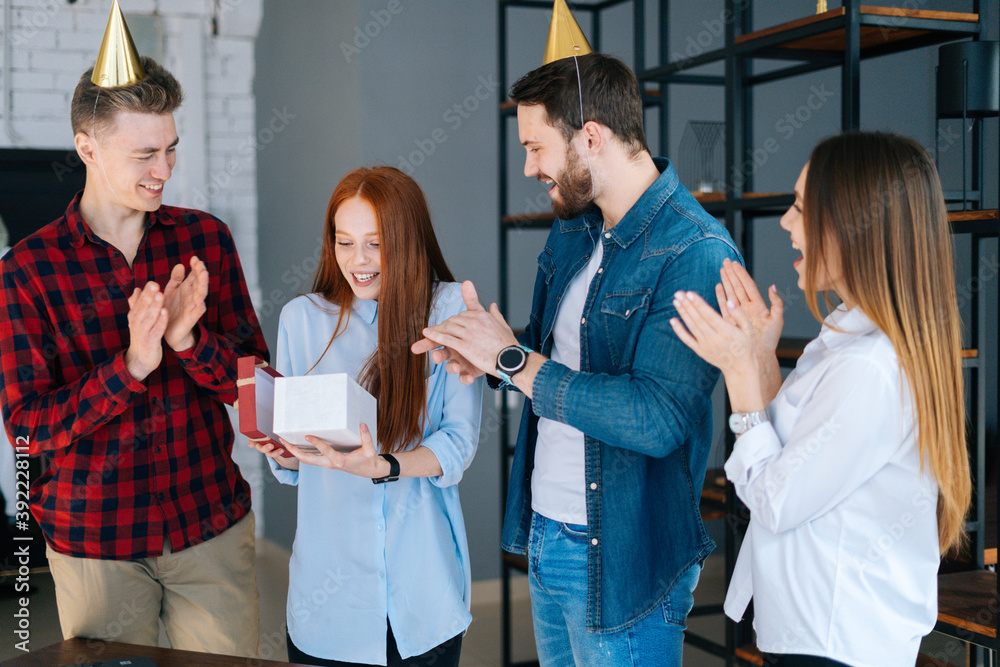 Foto de Cheerful red-haired young woman opening present given by ...