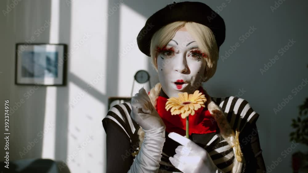 Portrait of pretty girl mime wearing funny costume and make-up smelling flower and smiling ...