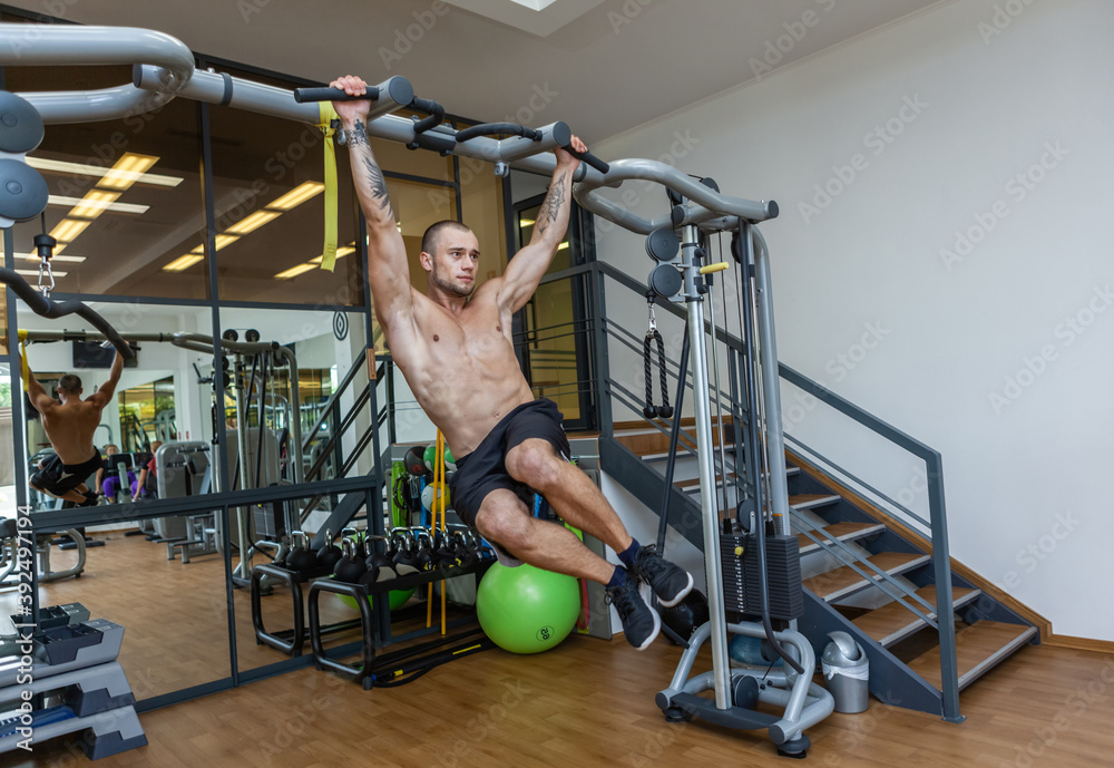 Young muscular fitness man training abdominal muscles while hanging on ...