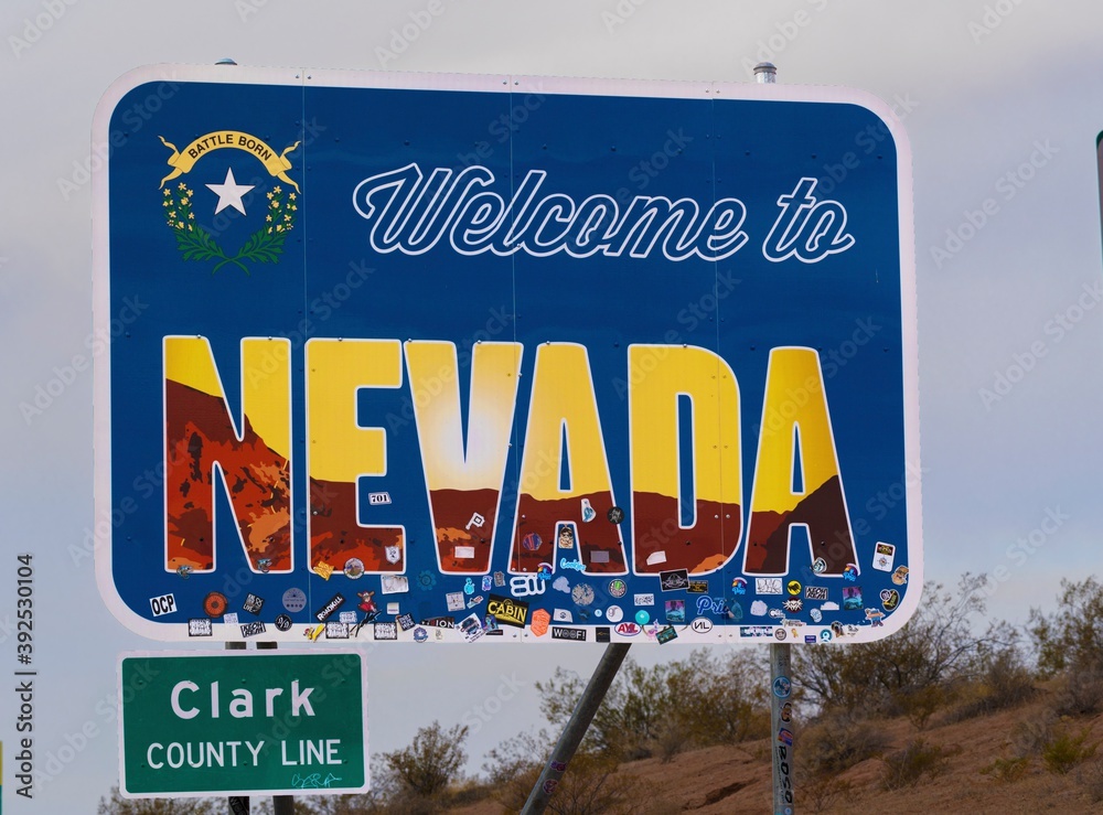 This image shows a "Welcome To Nevada" road side sign with blue skies ...