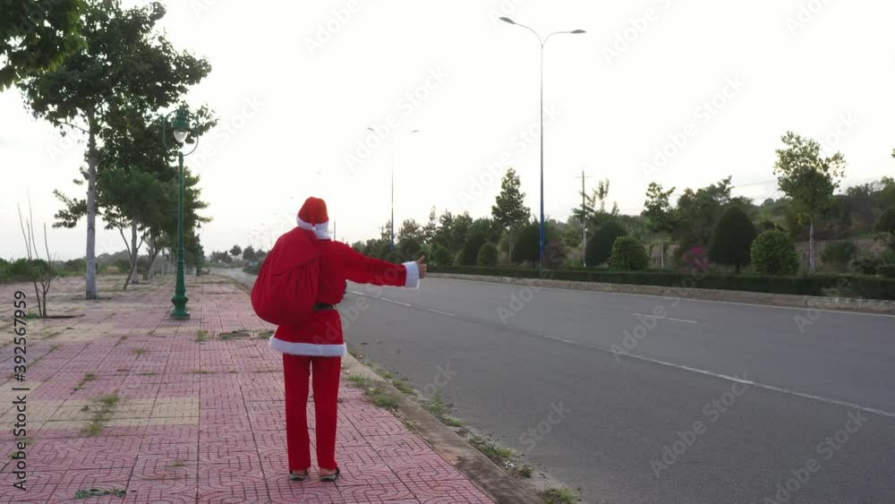 Santa is hitchhiking on the road with gift bag in summer sunset. New ...