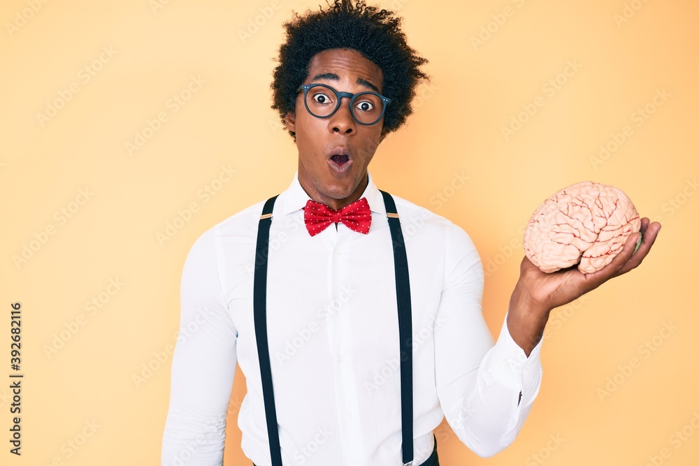 Handsome african american nerd man with afro hair holding brain scared ...