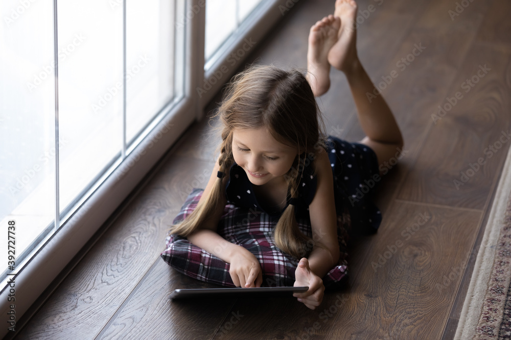 At home alone. Happy small girl lying on heated wooden floor enjoying ...