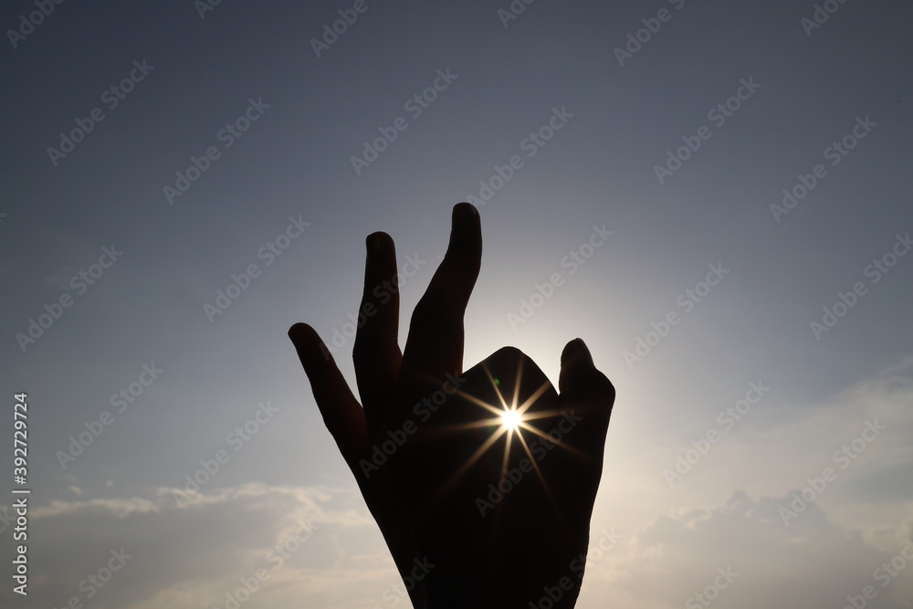 silhouette of a hand on the blue sky background with the sun in between ...