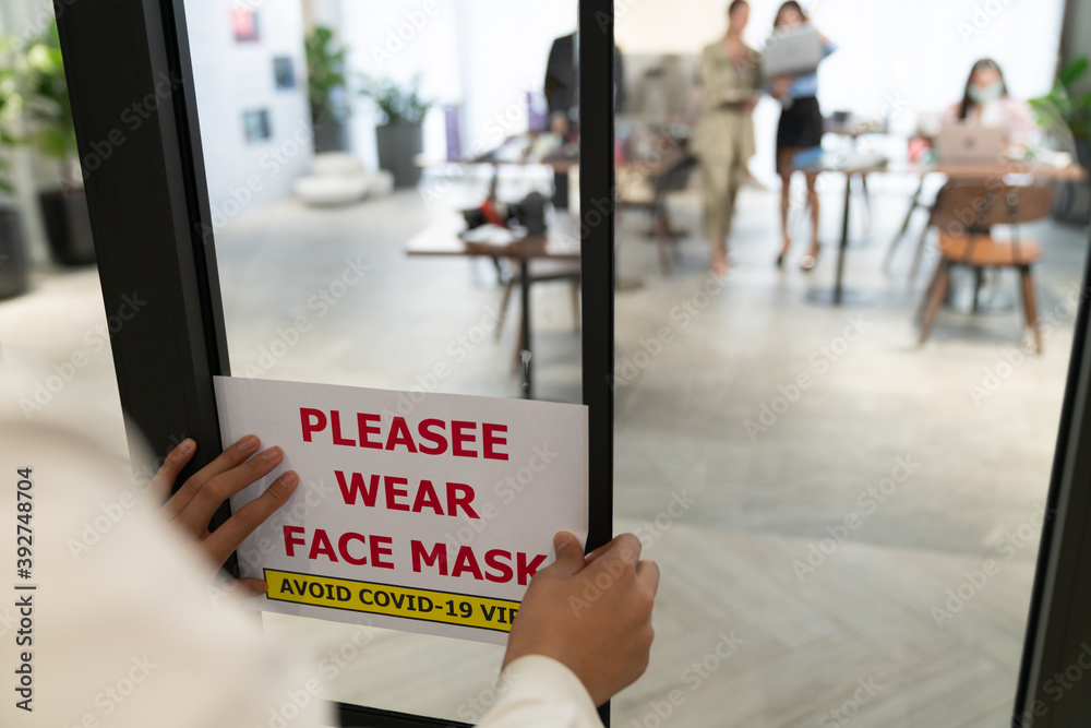 A businessman wearing a surgical mask puts an open sign "Open" at the ...