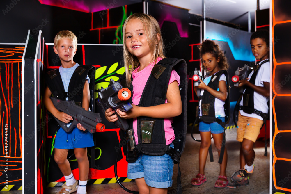 Cute preteen girl with a laser pistol playing laser tag with friends on ...