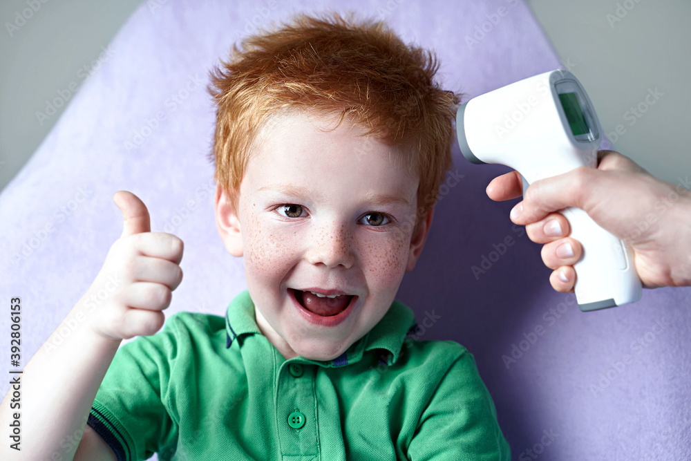 Doctor measures temperature of a cute red haired freckled little boy ...