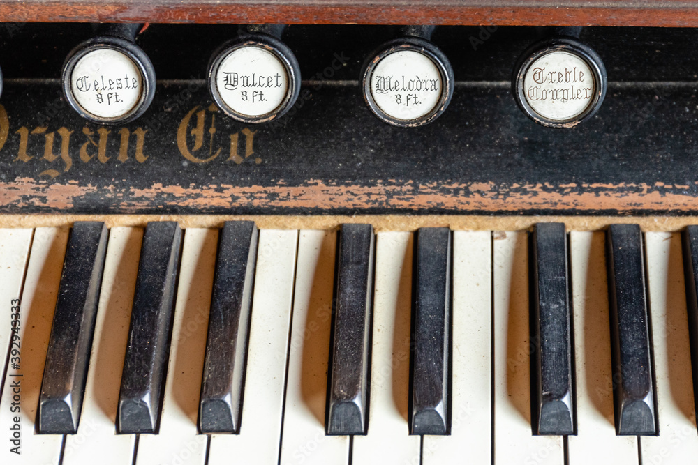 Organ stop handles on an old pump organ with worn black and white keys ...
