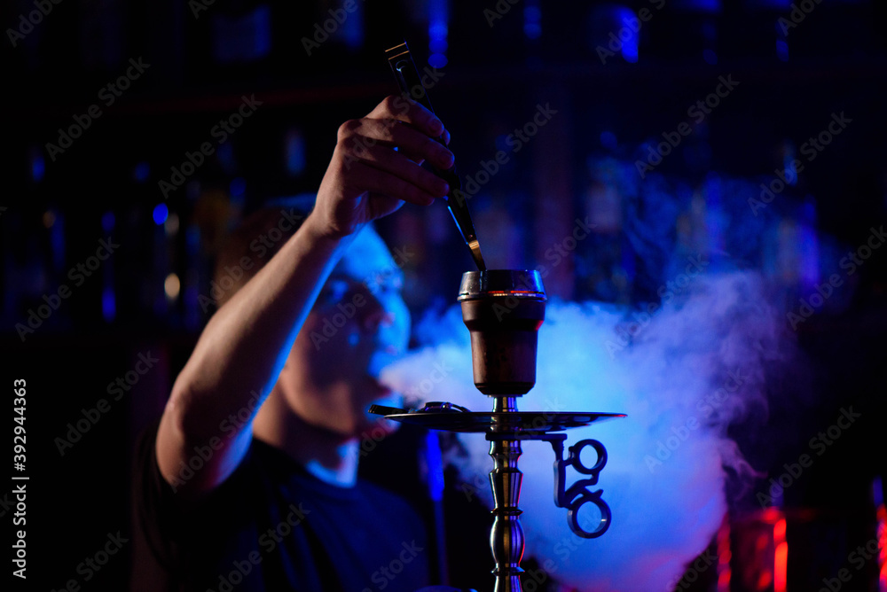 Man smoking traditional hookah pipe and exhaling smoke in hookah cafe ...