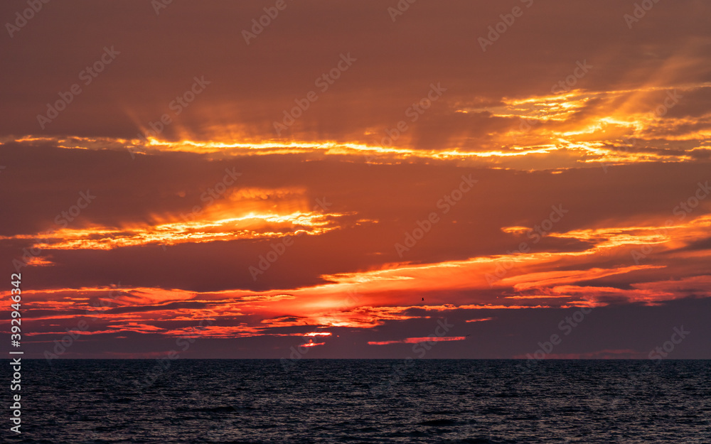 Light rays shining through clouds as the sun sets at ocean horizon ...