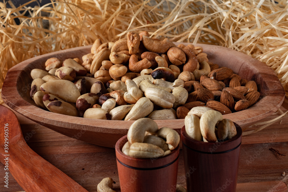 variety of nuts in a wooden bowl and in two wooden cups with straw ...