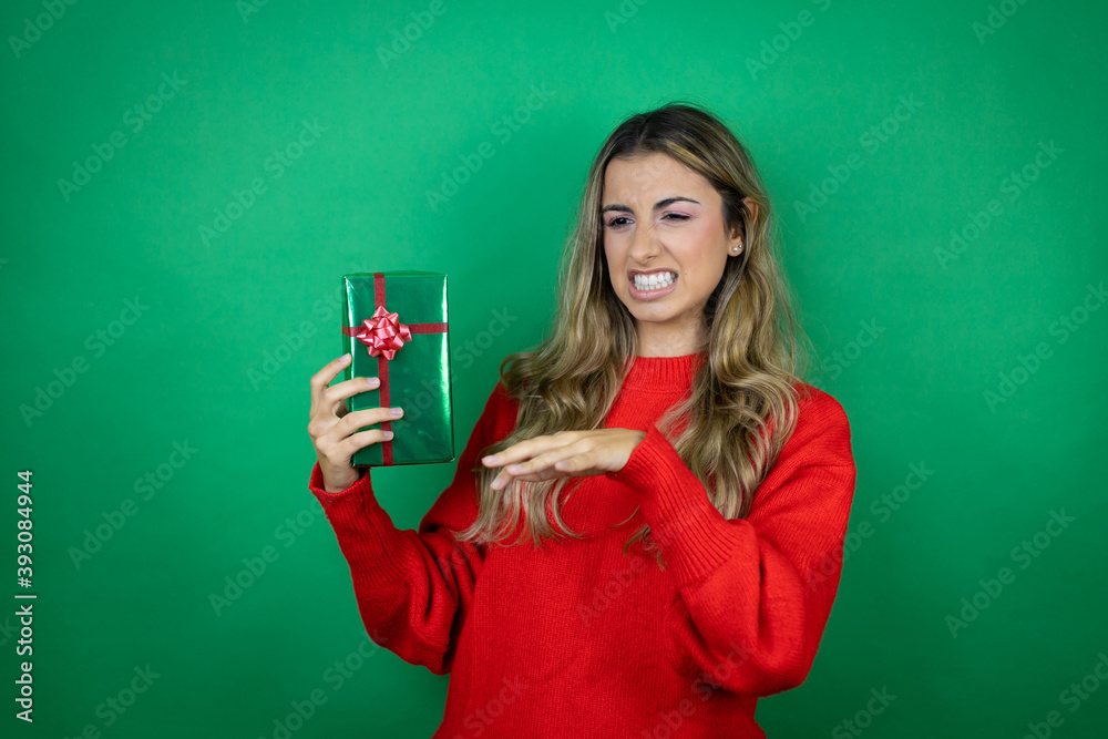 Young beautiful girl holding gift over isolated green background ...