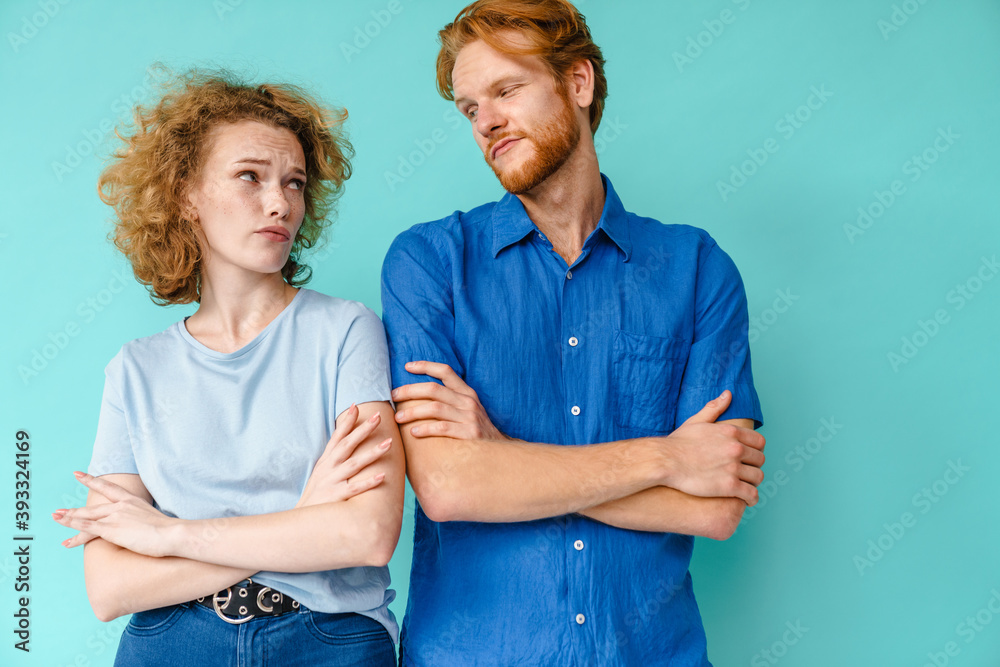 Confused couple looking at each other while posing with arms crossed ...