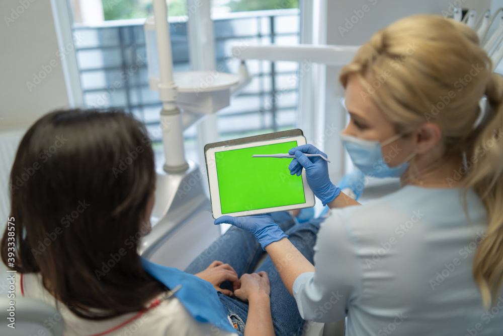 Female dentist showing female patient a tablet pc with treatment ...