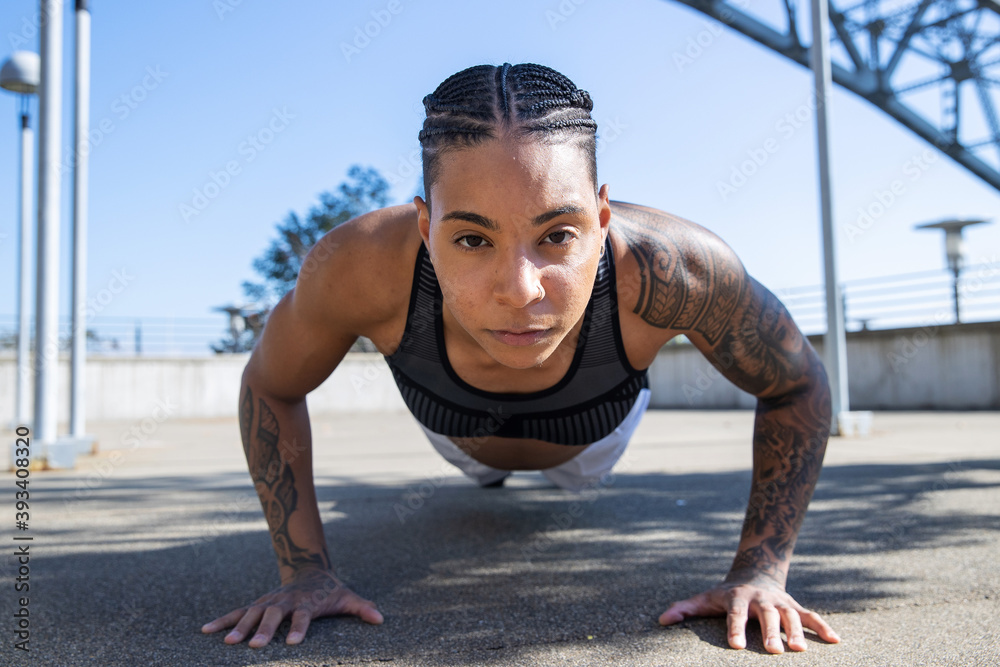 Strong black woman with tattoos doing pushups outside to build muscles ...