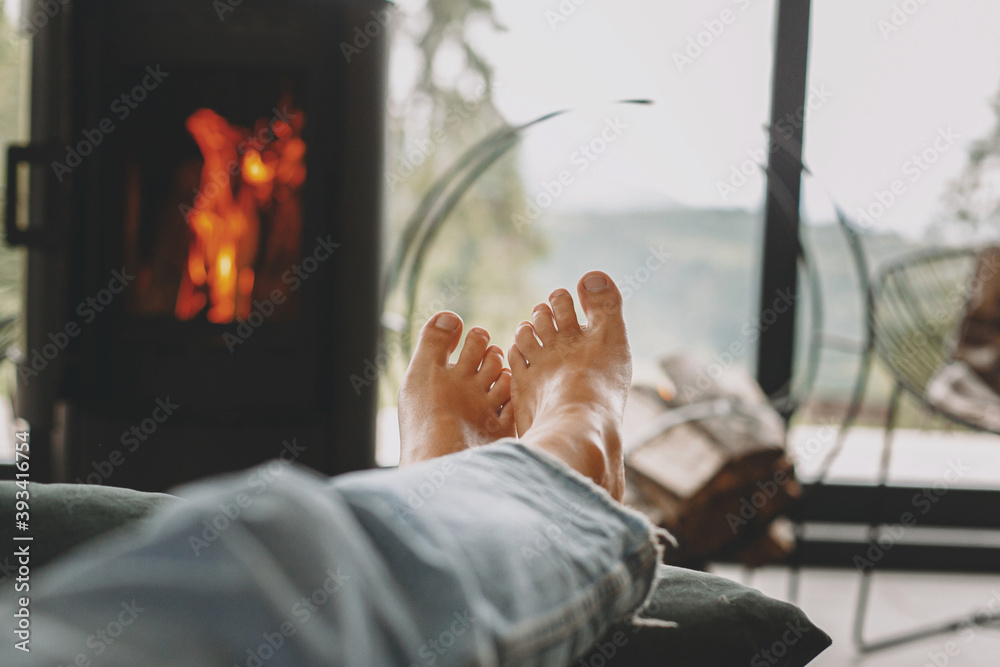 Feet at modern fireplace and window with view on mountains. Woman ...