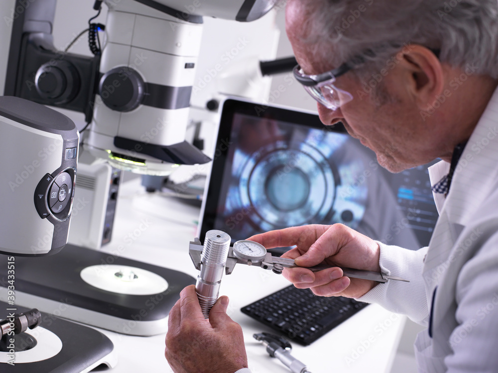 Engineer using a dial calliper and a 3d stereo microscope for quality ...