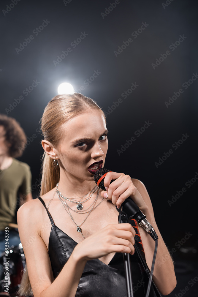 Angry blonde woman singing while touching microphone rack with backlit ...