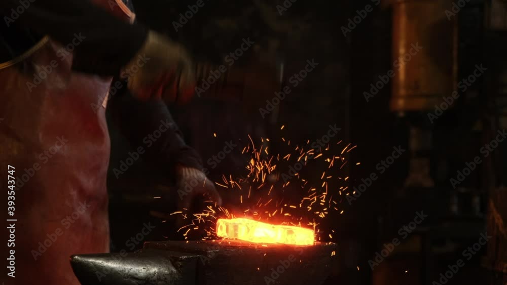 Medium shot of a man with a hammer hitting red-hot metal. A blacksmith ...