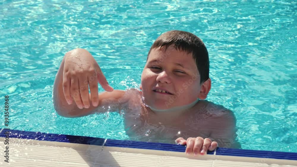 Cheerful fat kid boy showing thumb up in swimming pool with wet face ...