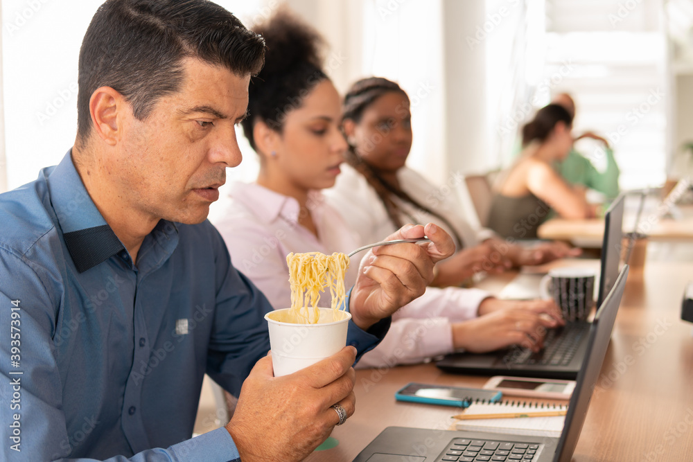 Brazilian senior man eating and working in office workspace. meal, busy ...