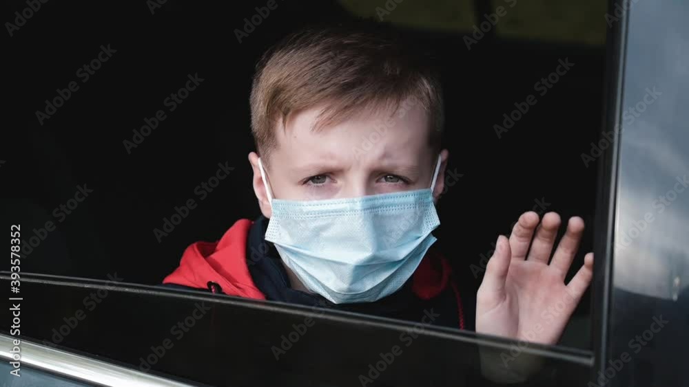 Young boy in a Medical Mask waving goodbye and looks through the car ...