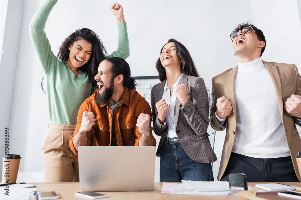 Excited hispanic office workers with yeah gesture standing near laptop ...