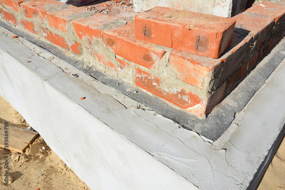 Laying a brick wall above the insulated foundation with a damp-proof ...
