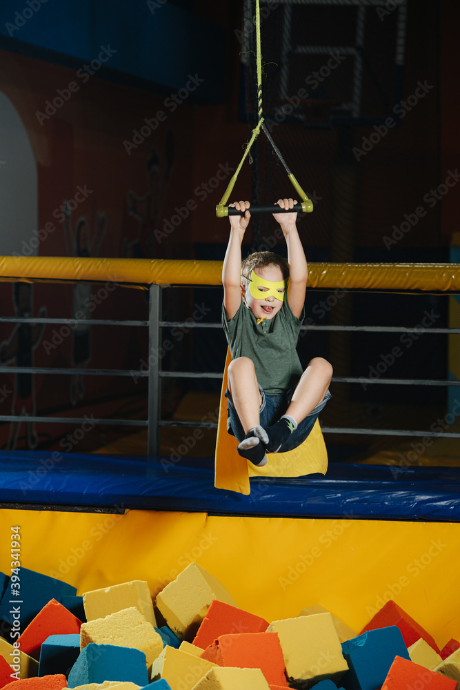 Masked little boy in a cape jumping in multi-color soft cube pool from ...