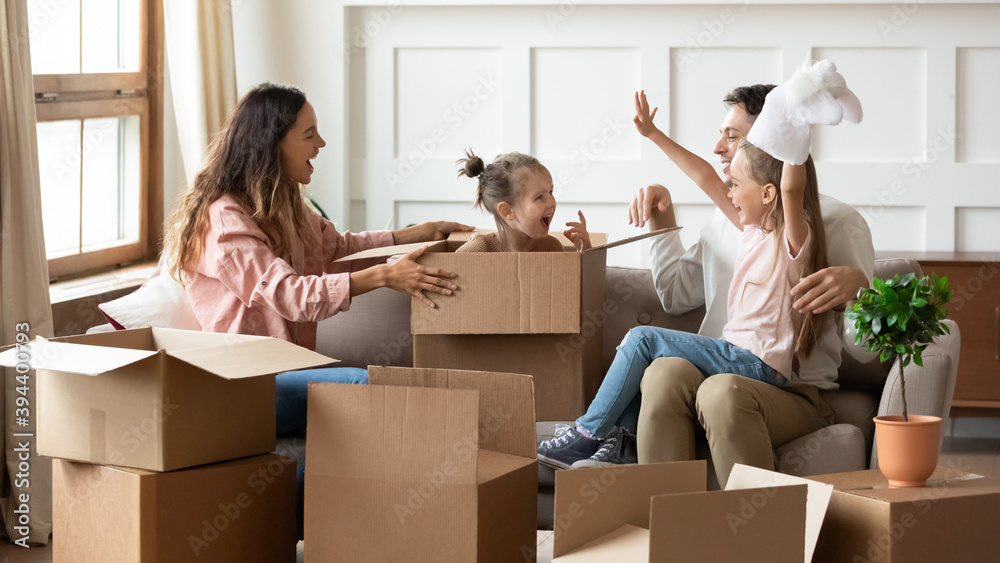 Little girl sit inside of big box play together with family at moving ...