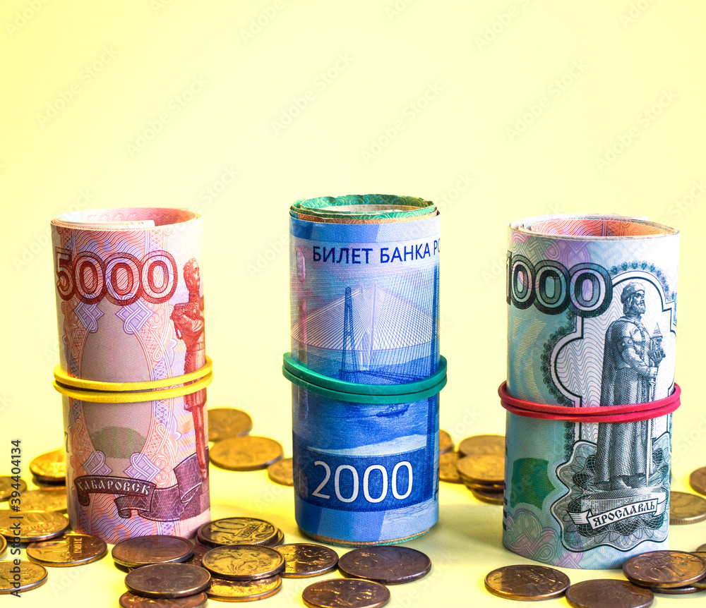 Russian rubles rolled into a tube and metal coins on a light background ...