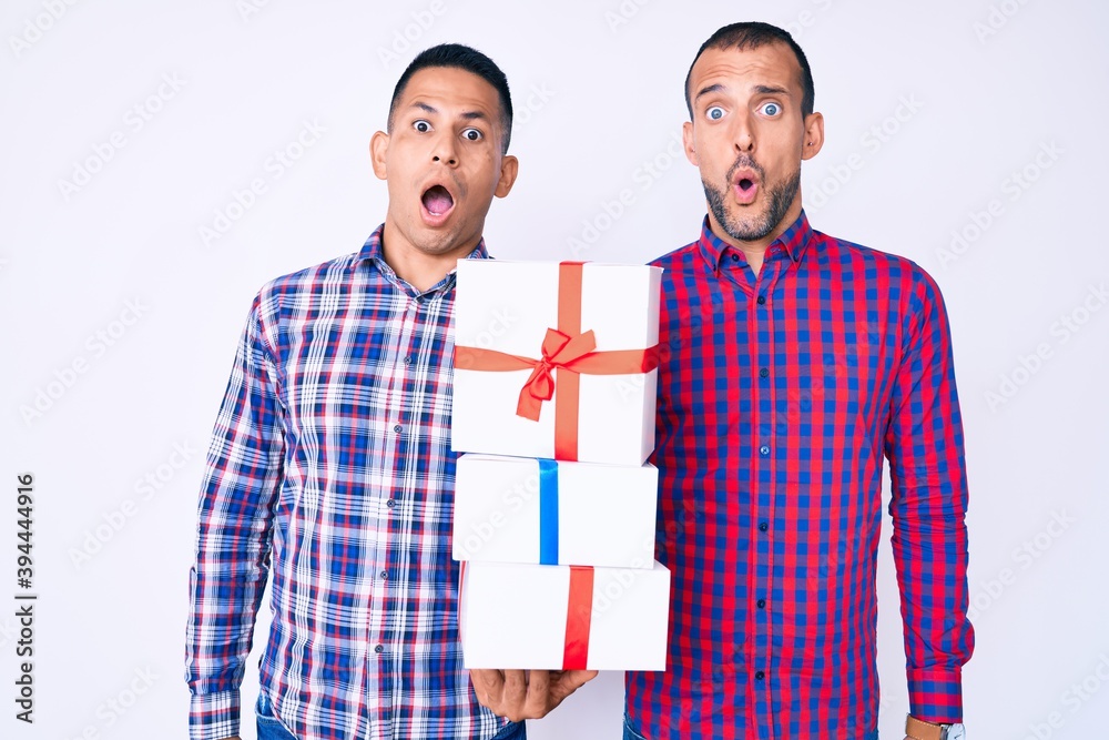 Young gay couple of two men holding gift scared and amazed with open ...