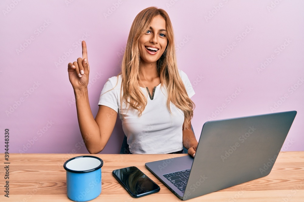 Beautiful blonde young woman working using computer laptop surprised ...