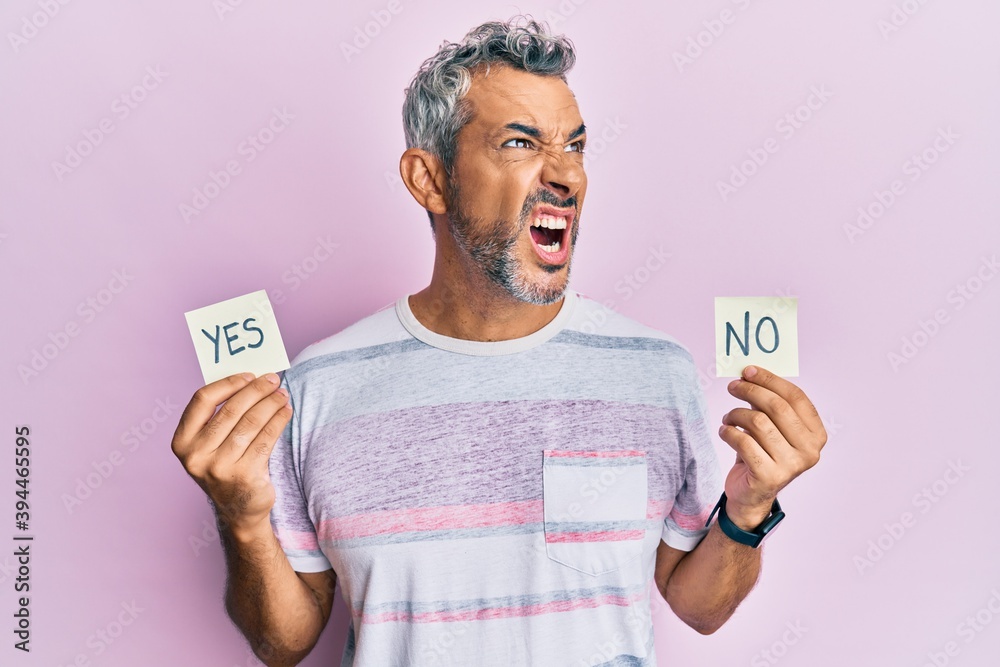 Middle age grey-haired man holding yes and no reminder angry and mad ...