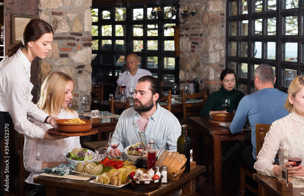 Polite waitress bringing ordered dishes to guests in comfortable ...