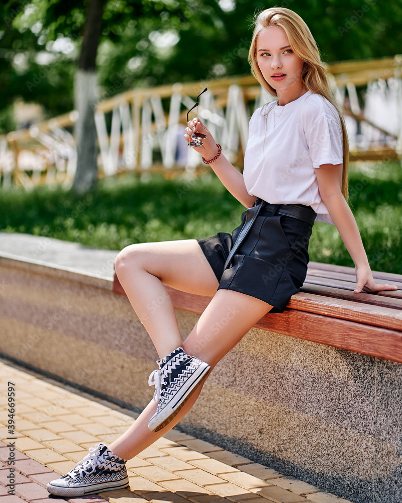 teenage girl sitting on a bench in a city park, legs crossed. vertical ...