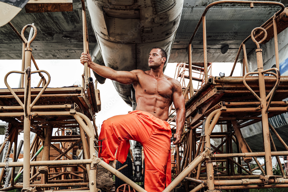 Bodybuilder mechanic in orange uniform with naked torso poses under ...