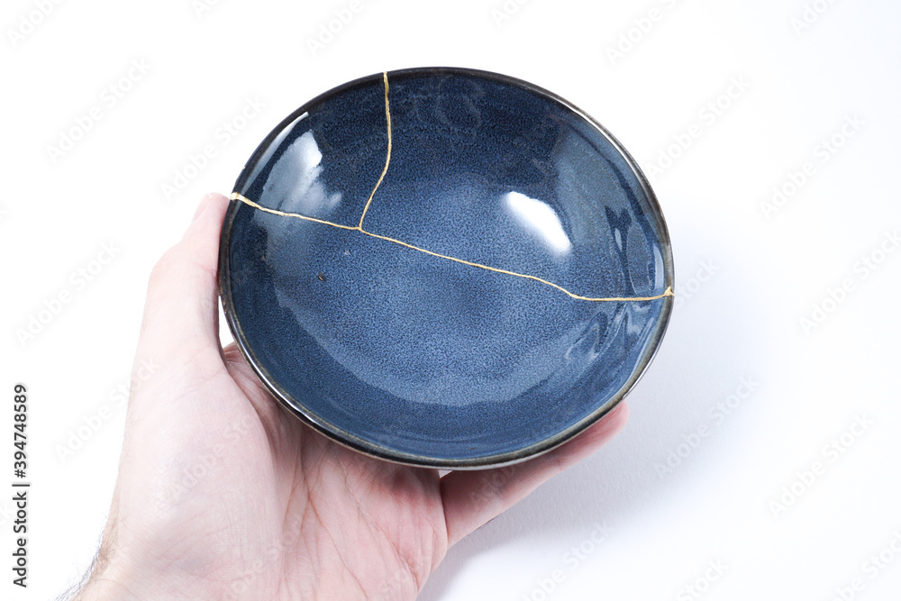 Hand holding kintsugi bowl. Gold cracks restoration on pottery restored ...