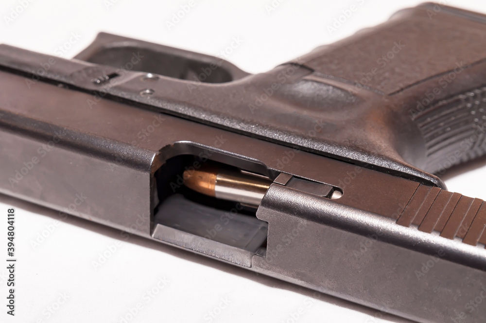 A black 9mm pistol with it's slide open showing a bullet about to be ...