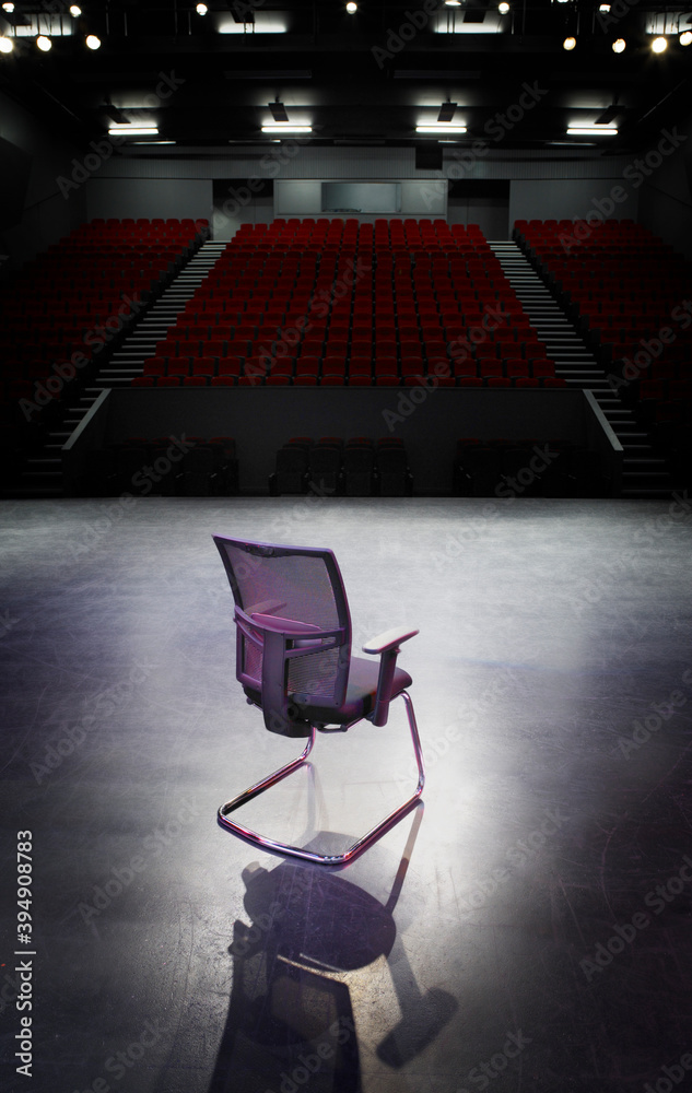 Back view of empty chair lit up on stage looking out towards empty ...