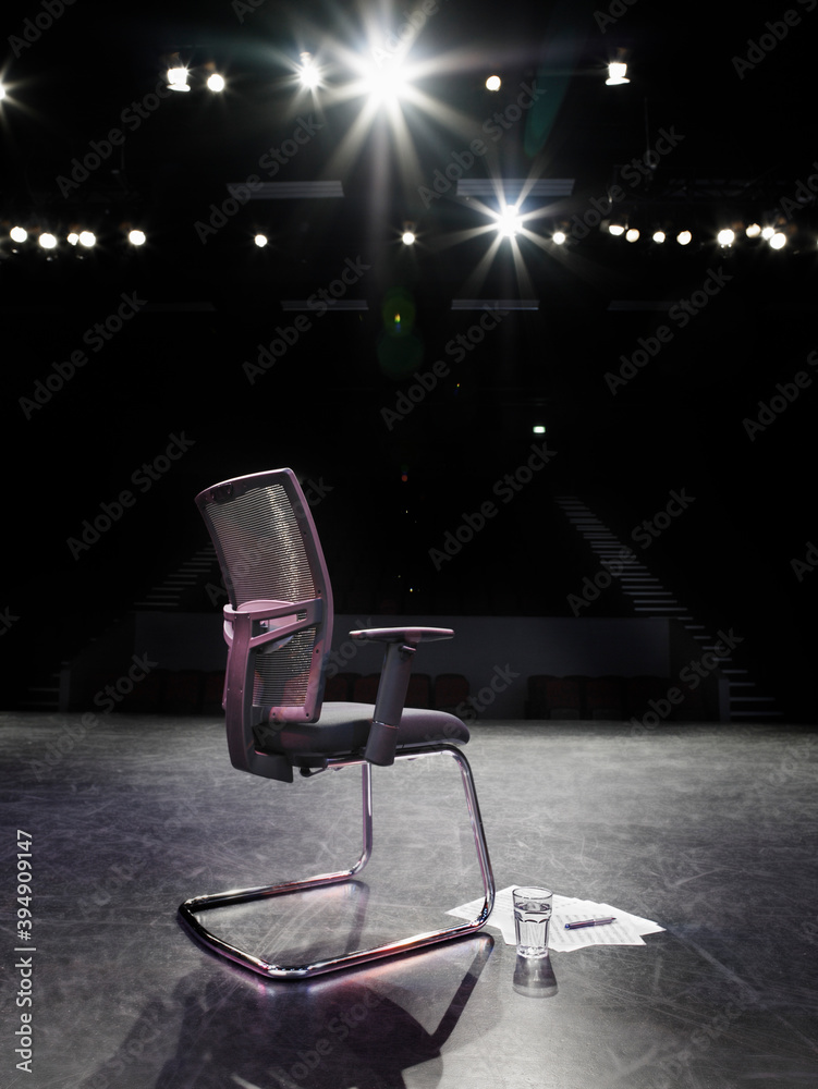 Back view of spotlit empty chair on stage with script and glass of ...