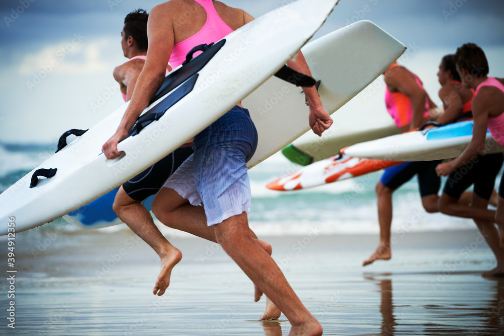 Close up of team of male surf lifeguards training and running into sea ...