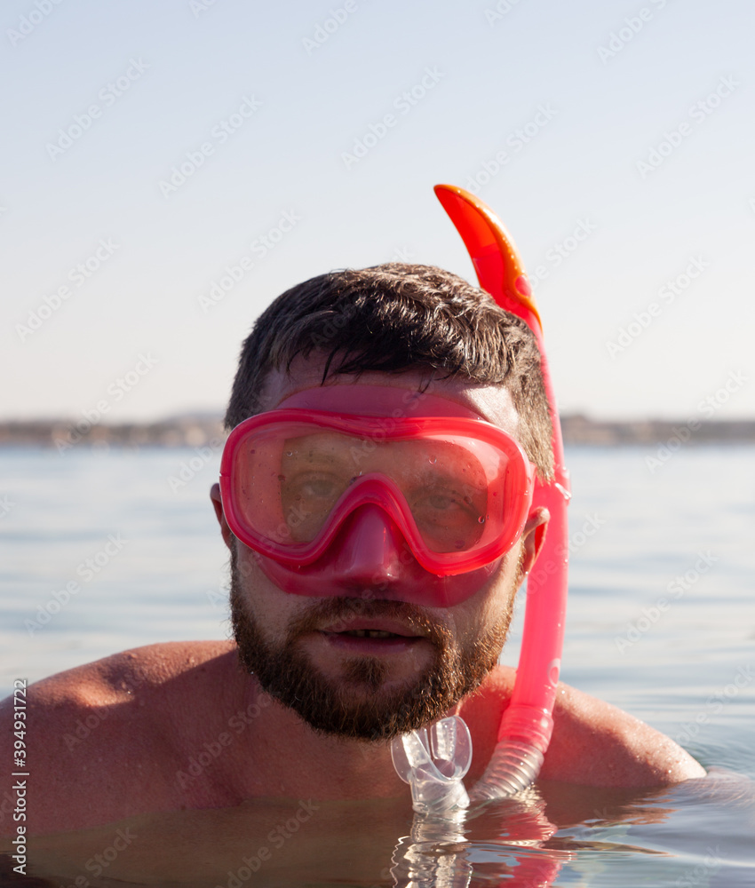 Young masculine man in a pink mask and snorkel in the water in the sea ...