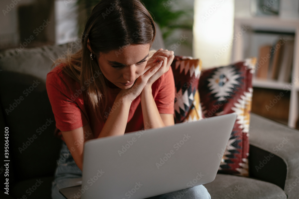 Worried woman using laptop. Young sad woman sitting in the living room ...